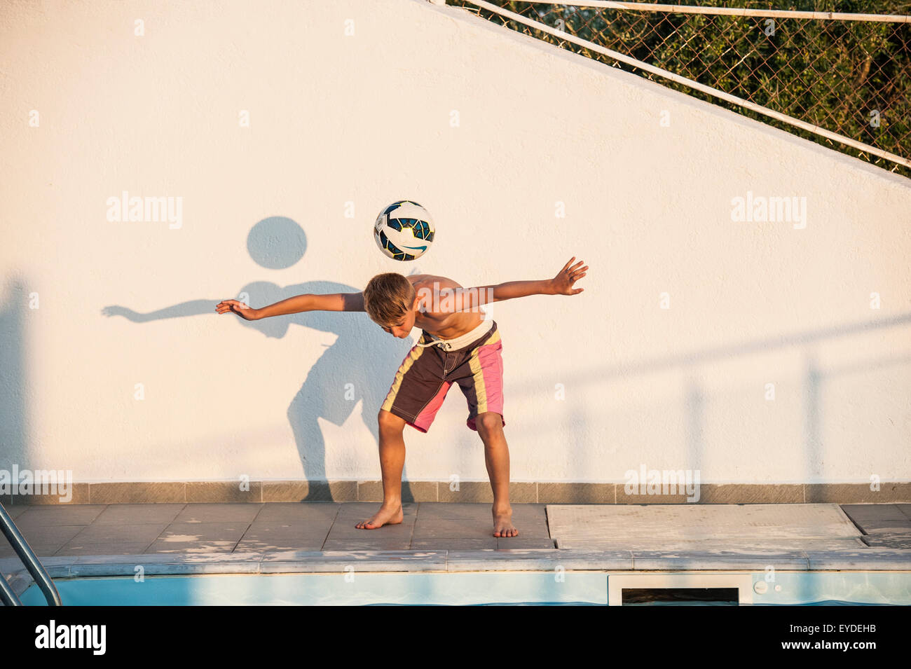 A boy playing football on holiday by a swimming pool Stock Photo - Alamy