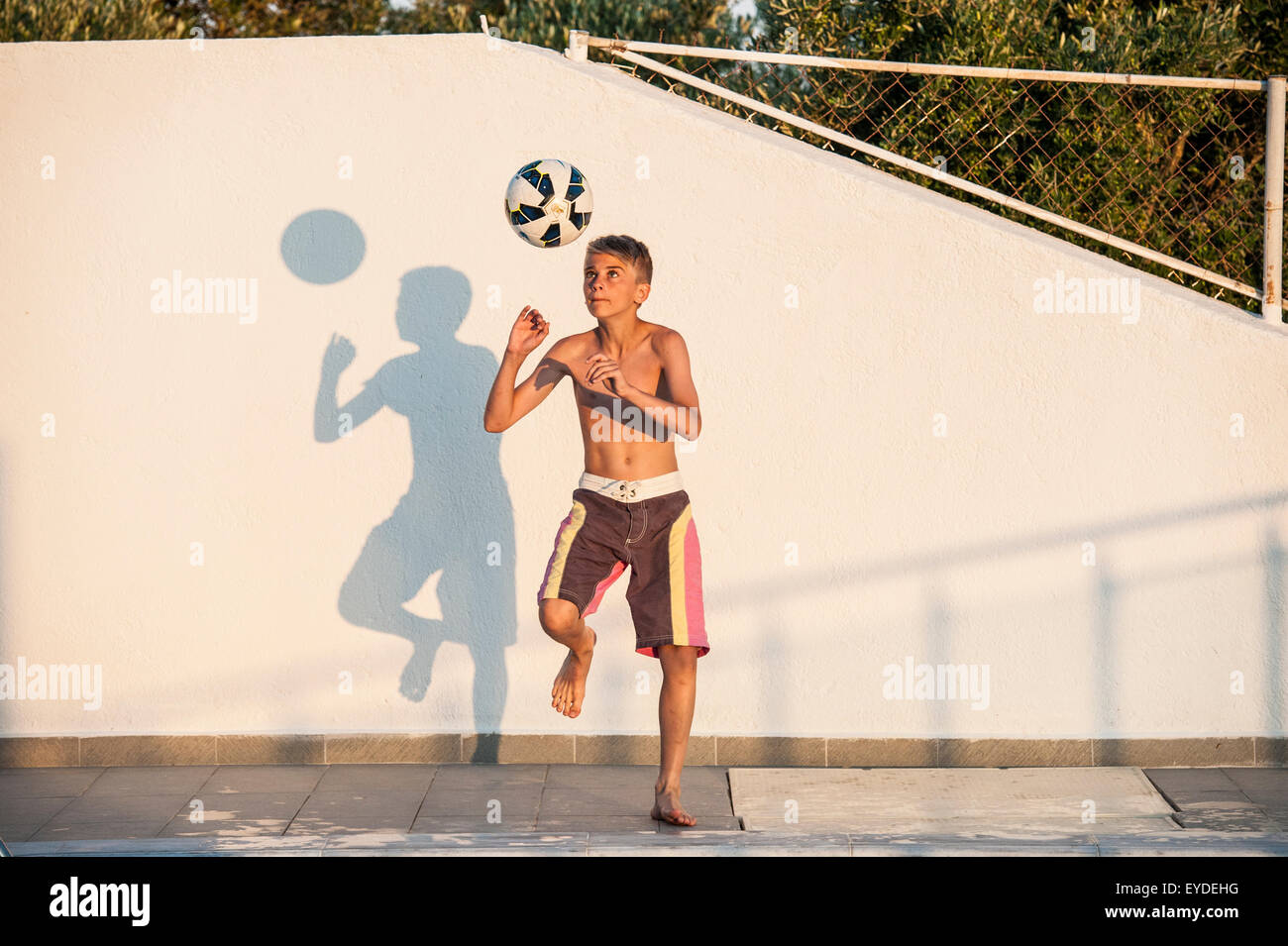 A boy playing football on holiday by a swimming pool Stock Photo - Alamy