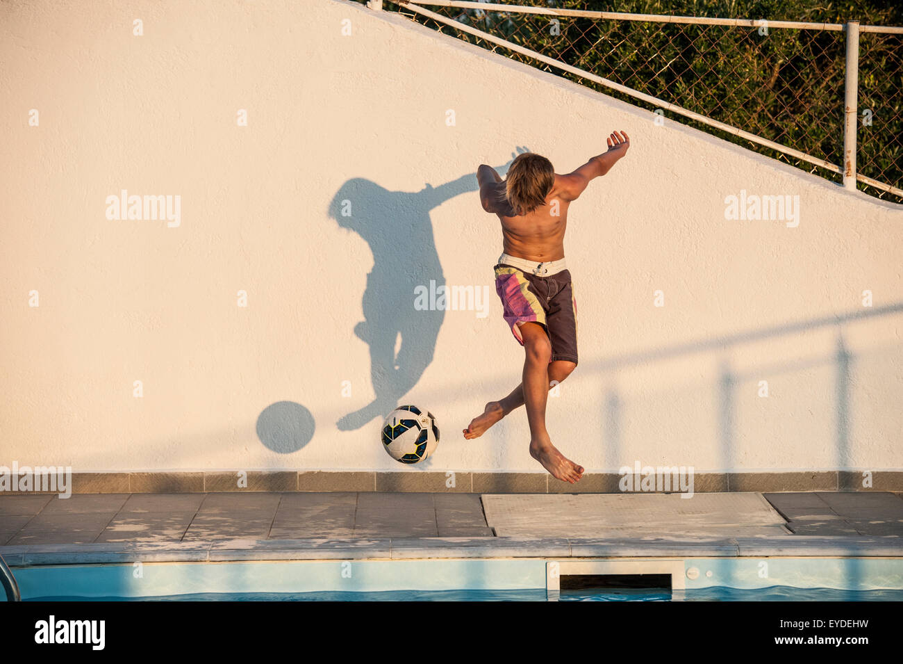 A boy playing football on holiday by a swimming pool Stock Photo - Alamy