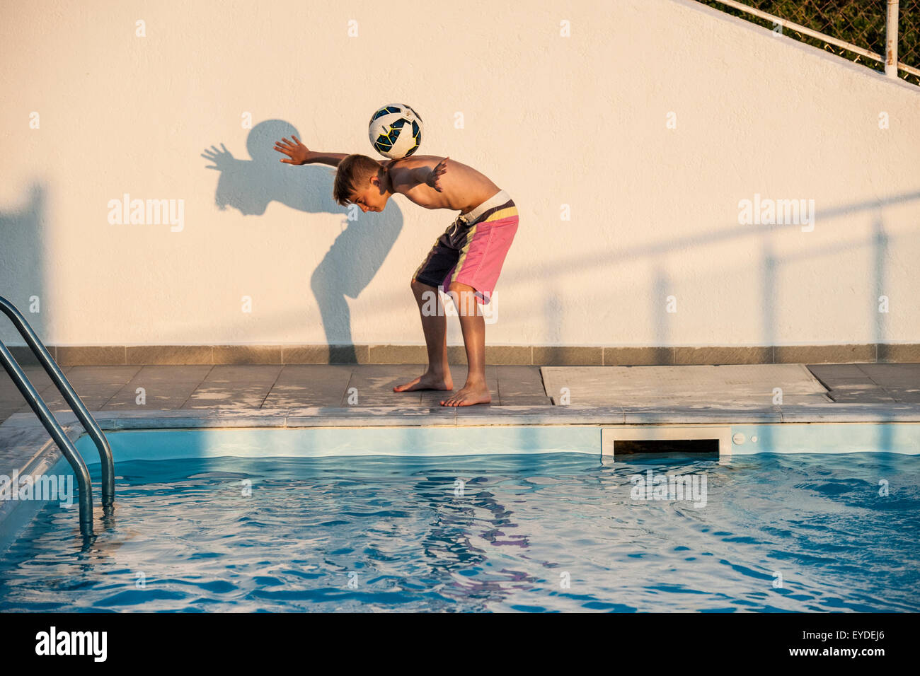 A boy playing football on holiday by a swimming pool Stock Photo - Alamy