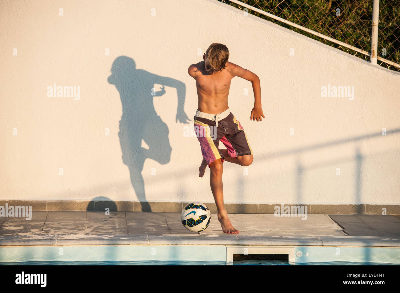A boy playing football on holiday by a swimming pool Stock Photo - Alamy
