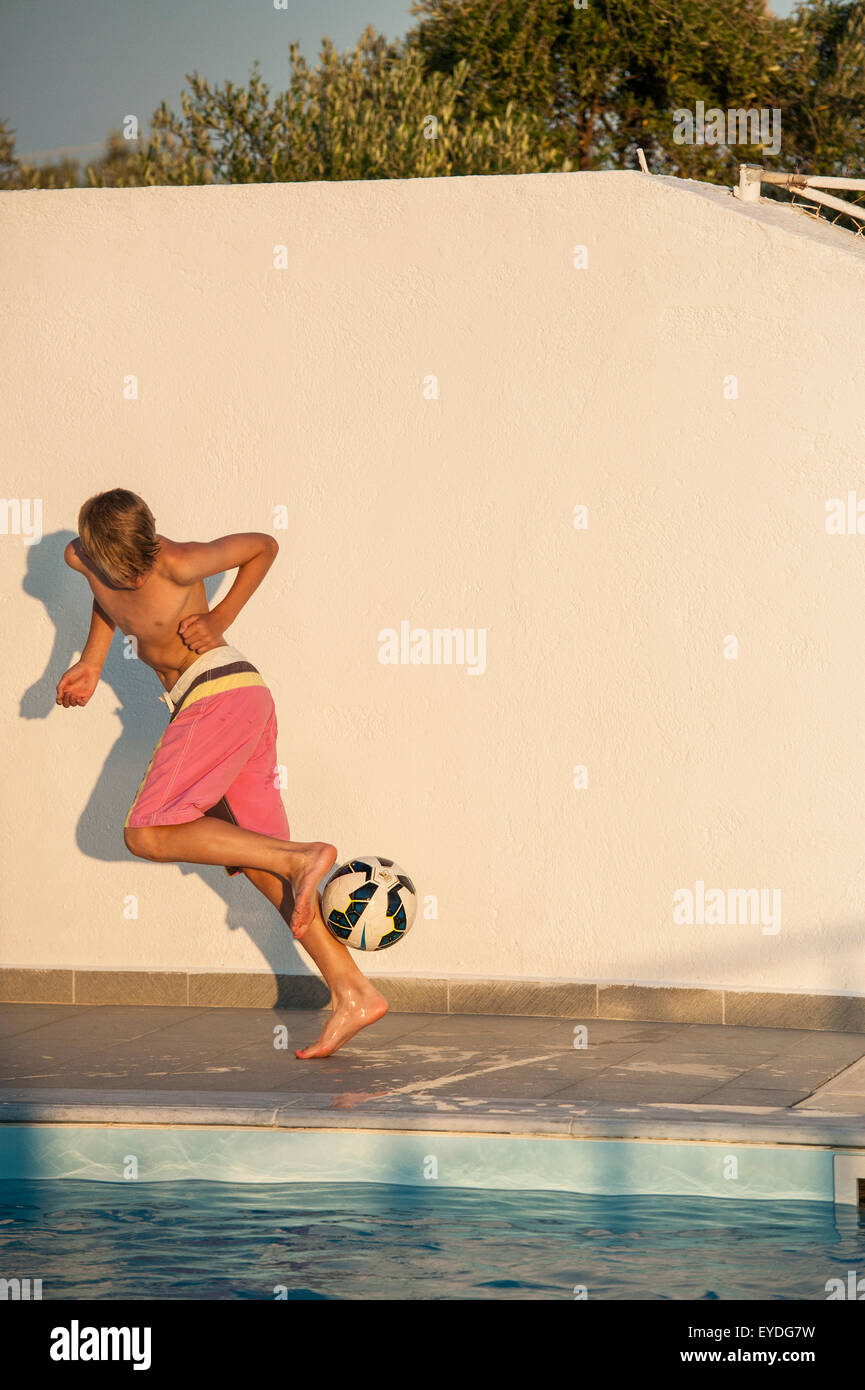 A boy playing football on holiday by a swimming pool Stock Photo - Alamy