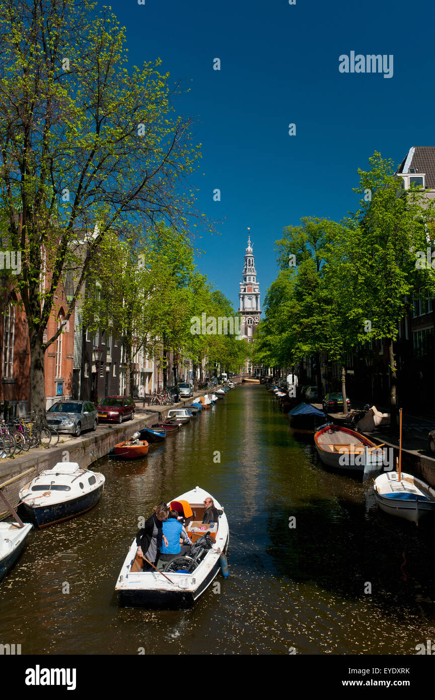 Holland, People in small boat going along small canal with spire of the ...