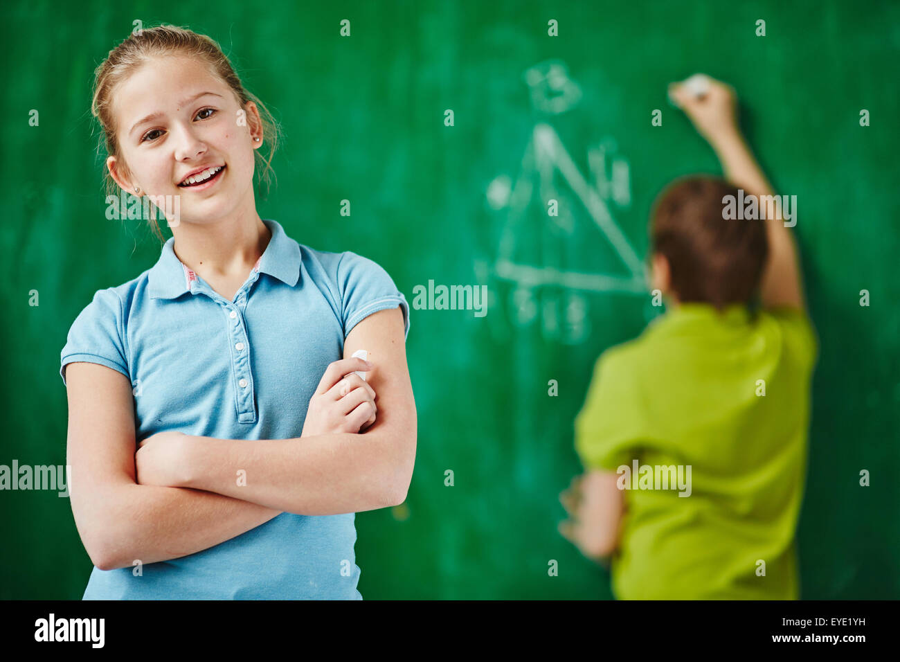 Successful schoolgirl looking at camera on background of classmate ...