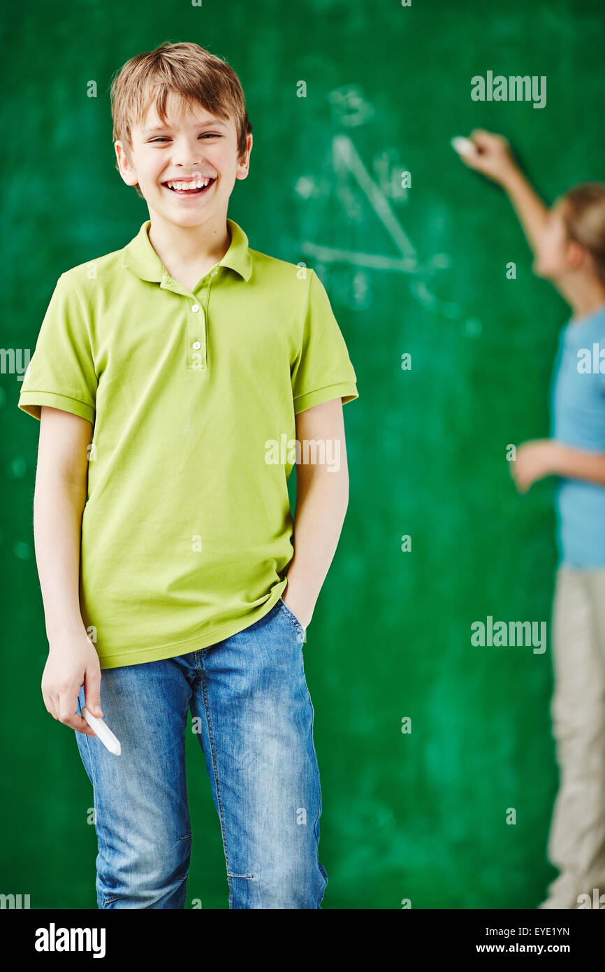 Cheerful schoolboy looking at camera on background of classmate by ...