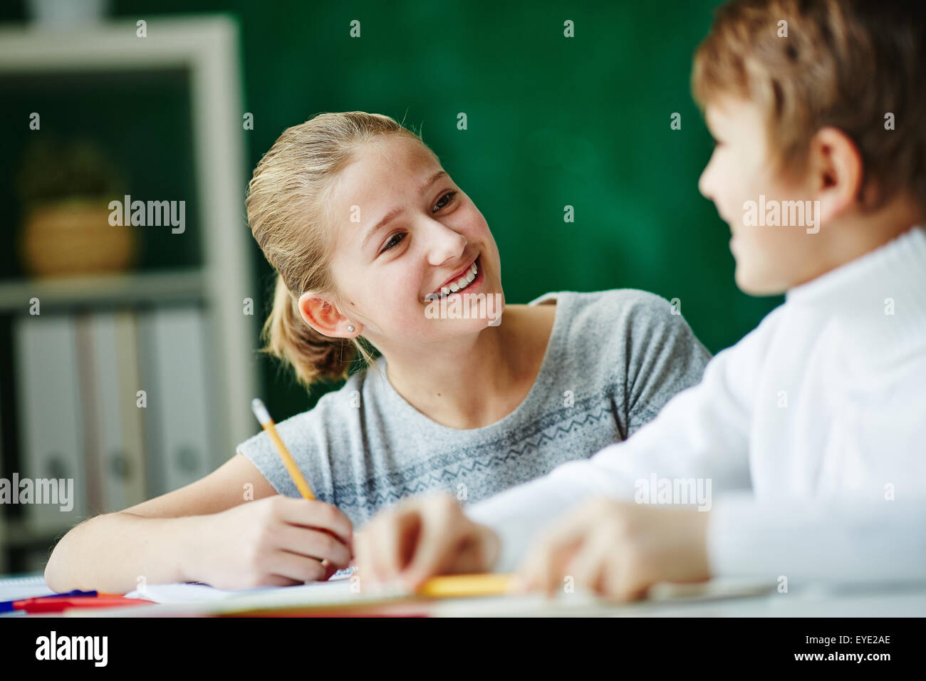 Happy schoolgirl looking at classmate while drawing Stock Photo - Alamy