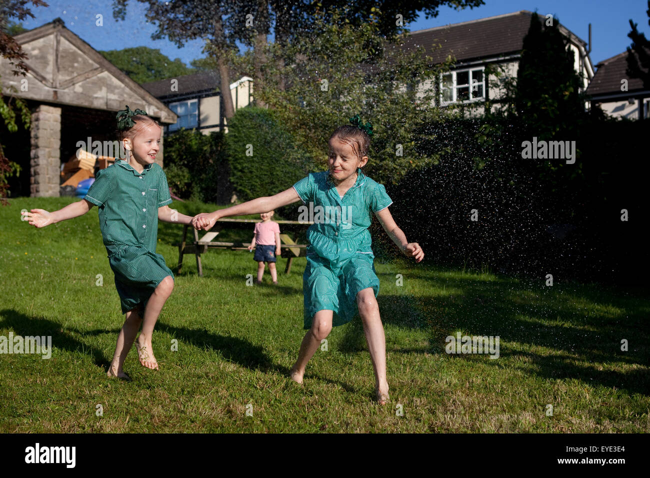 Two children in school dresses running through a water sprinkler Stock ...