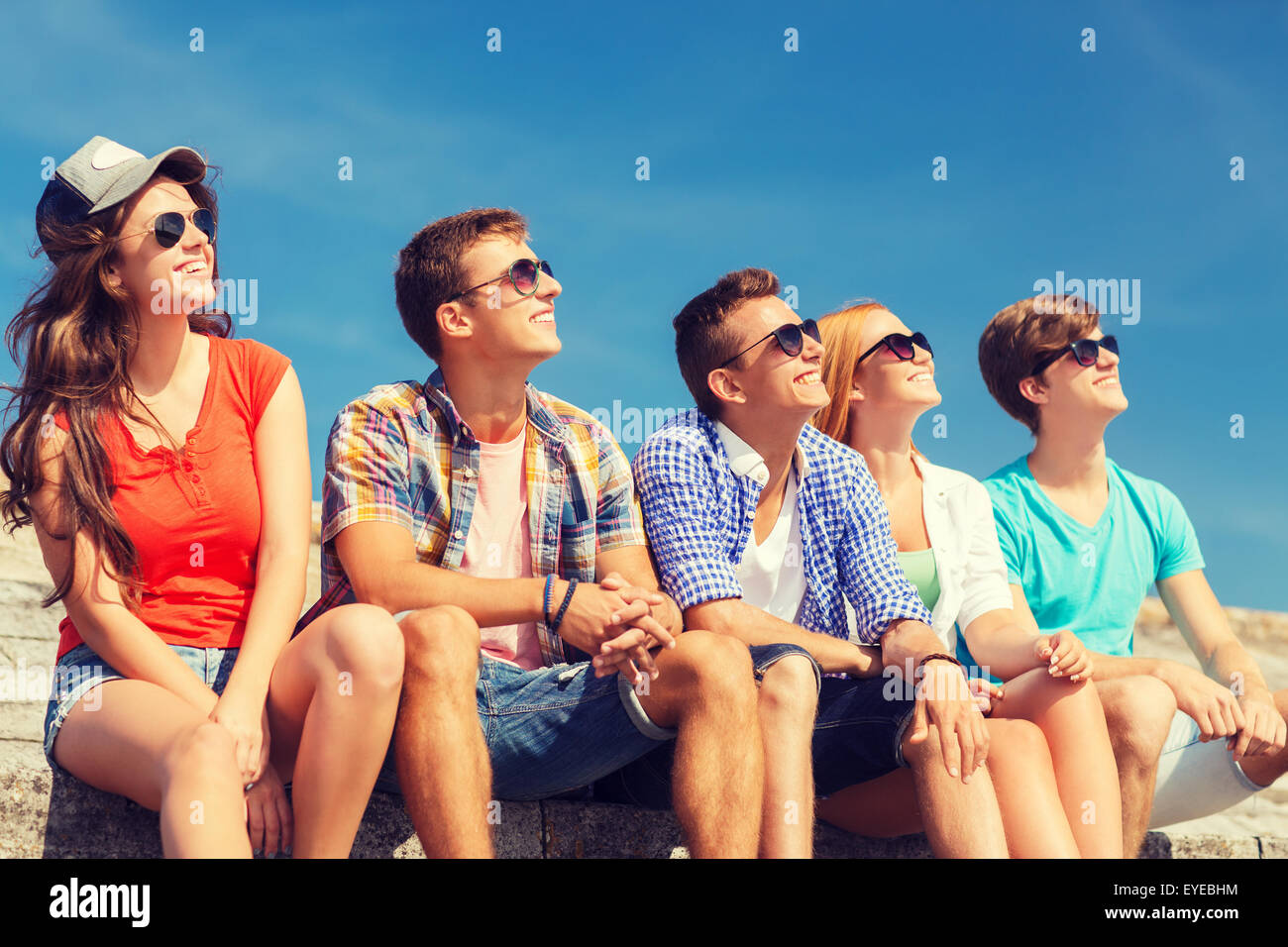group of smiling friends sitting on city street Stock Photo - Alamy