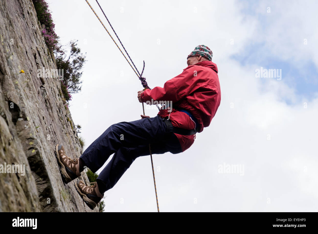 Novice male rock climber abseiling with safety rope on a rockface ...