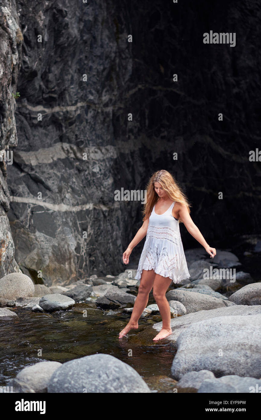 A young blond woman in a white, summer dress dipping her toe in the ...