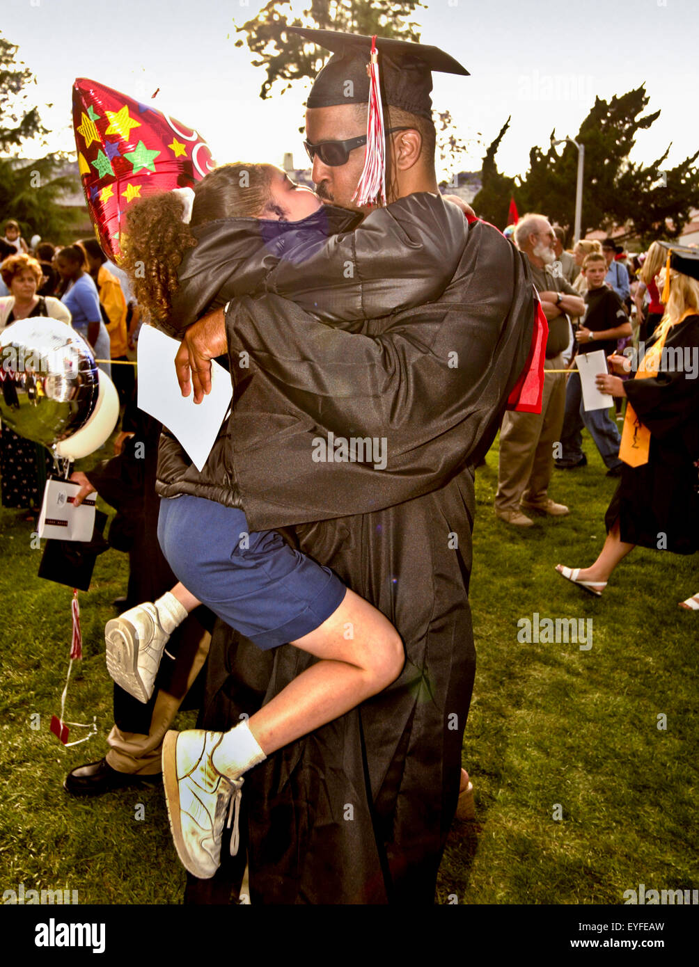 A happy community college graduate kisses his daughter at commencement ...