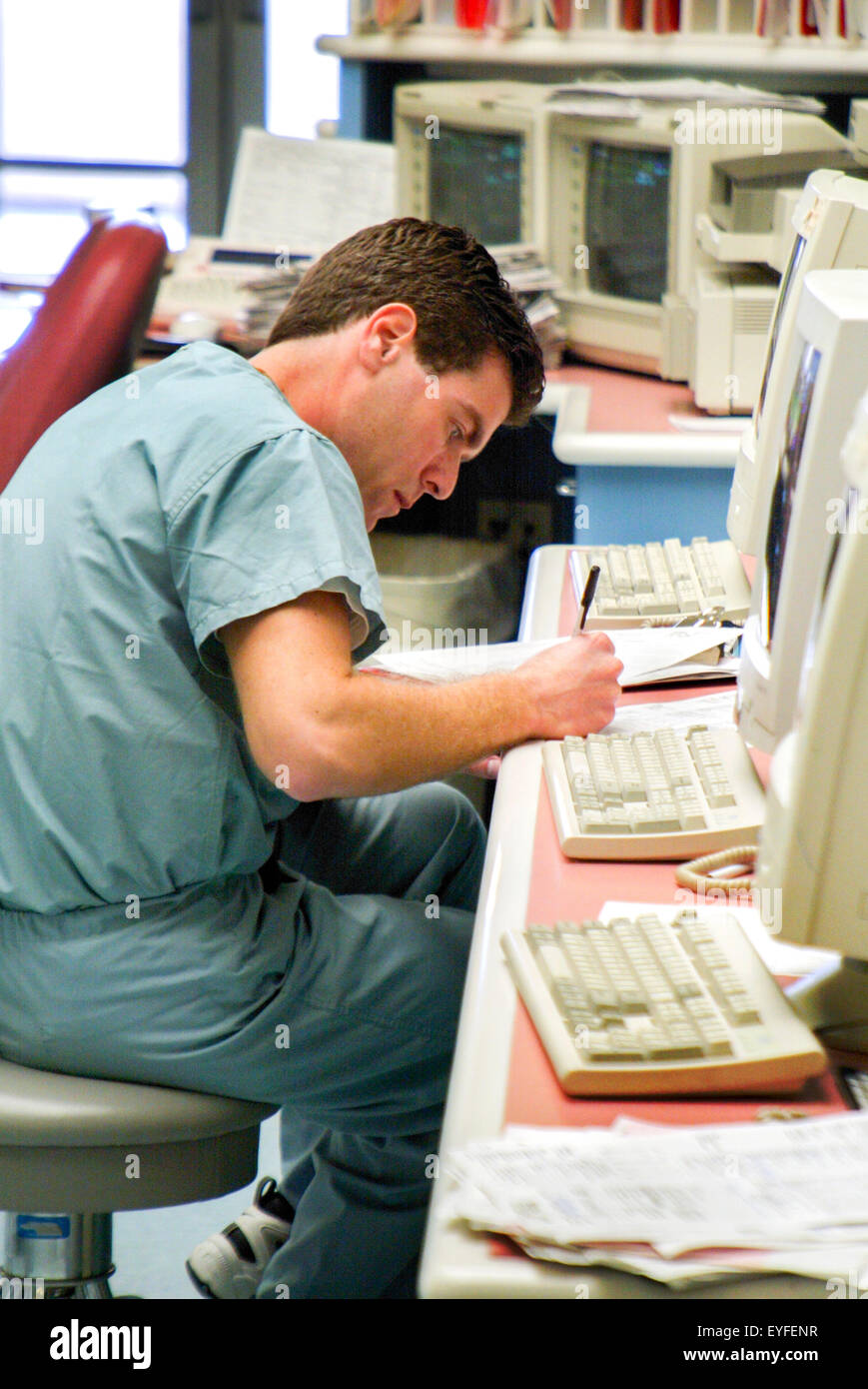A doctor makes patient notes at an emergency room nurse station in an ...
