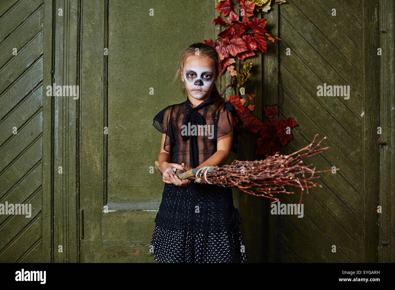 Little witch with painted face holding broom and looking at camera in ...