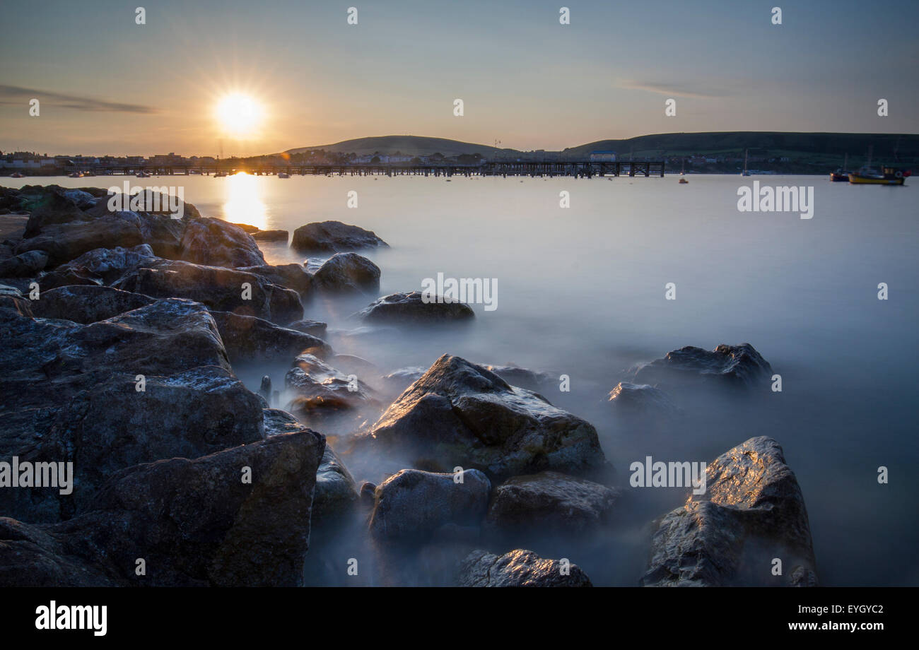 long exposure of sun setting over rocks in bay at Swanage Stock Photo ...
