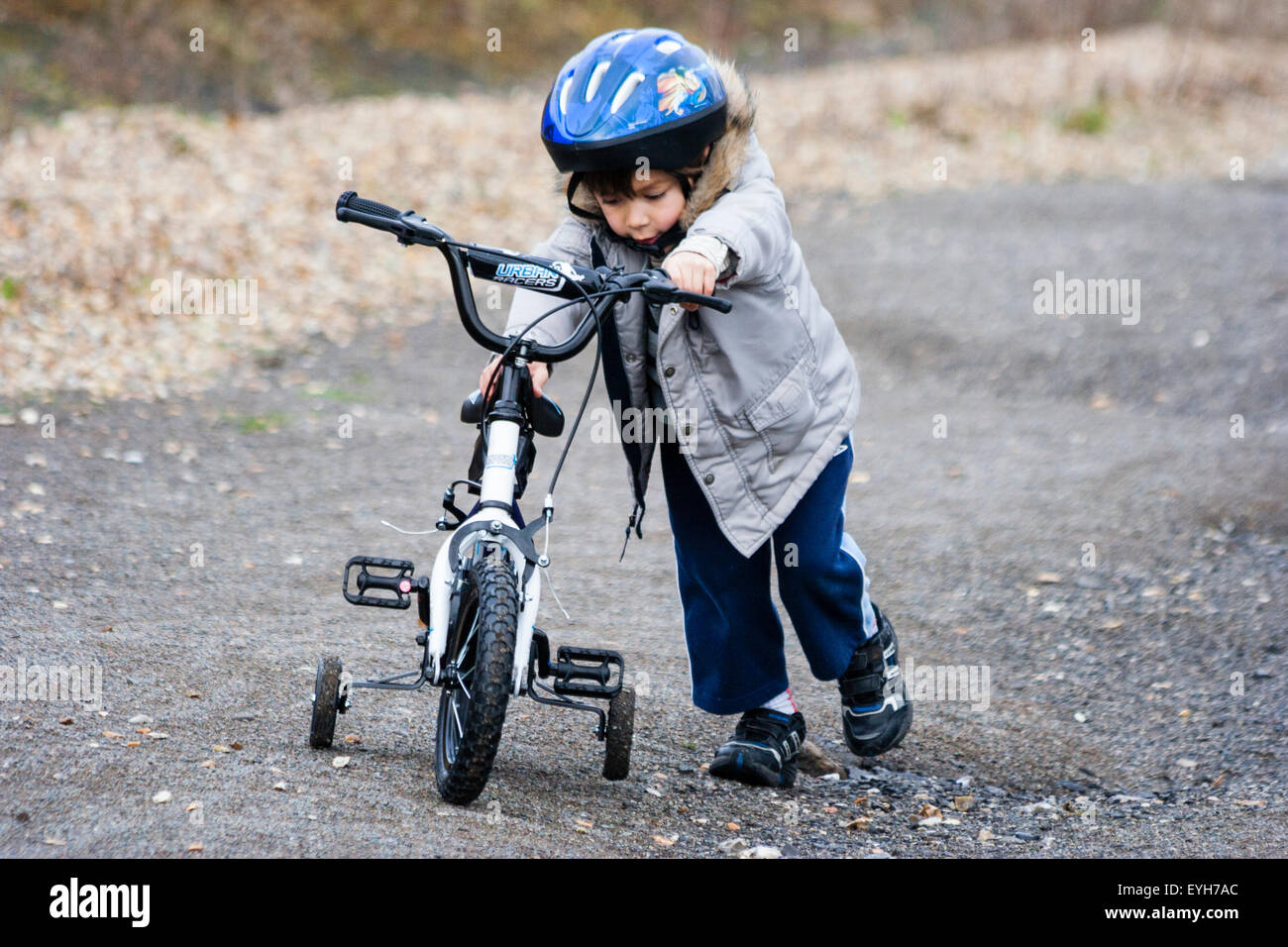 Boy struggling to push bicycle with stabilizers, up rough track in the ...