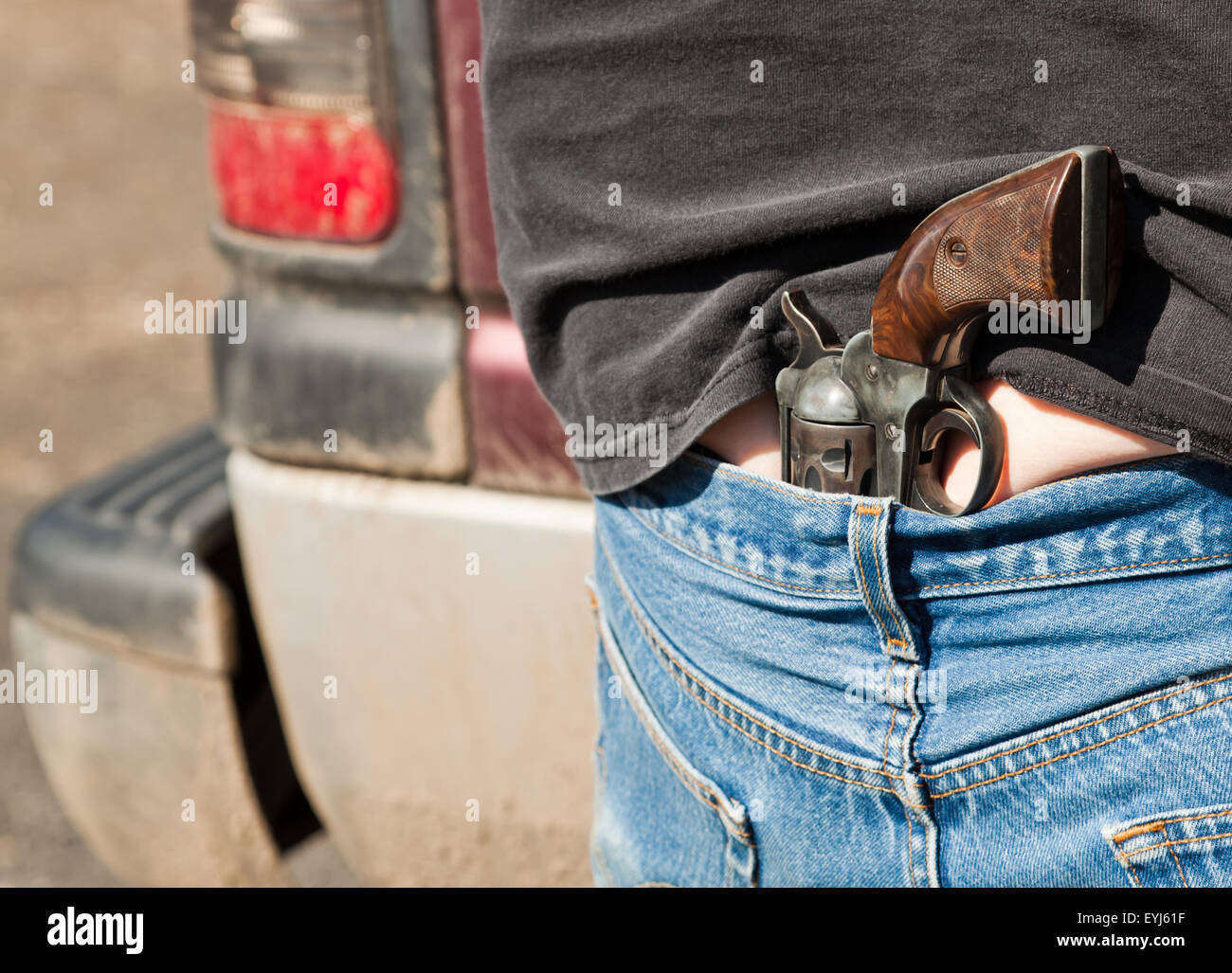 A well worn revolver with a wooden grip is tucked into a mans jeans ...