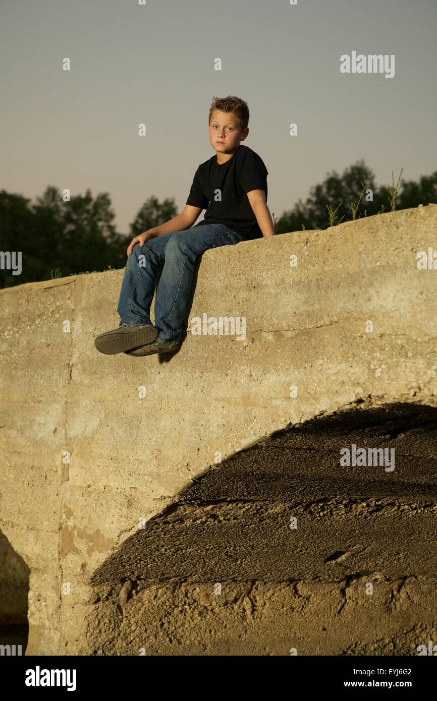 Boy sitting on bridge, reflecting alone Stock Photo - Alamy