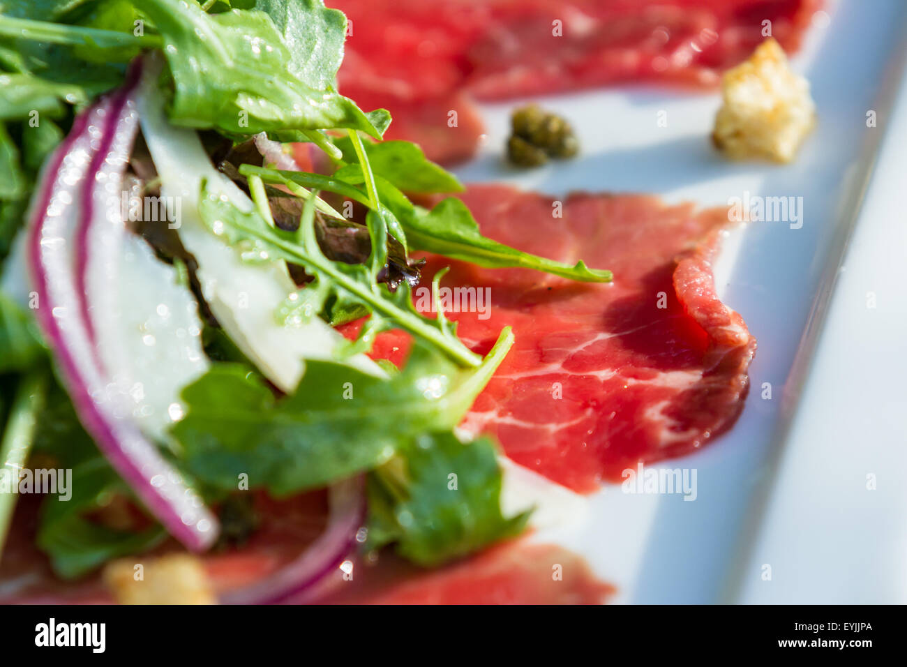 close up of a beef carpaccio appetizer served with an arugula salad as ...