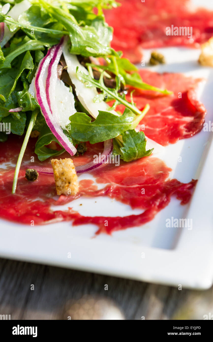 close up of a beef carpaccio appetizer served with an arugula salad as ...
