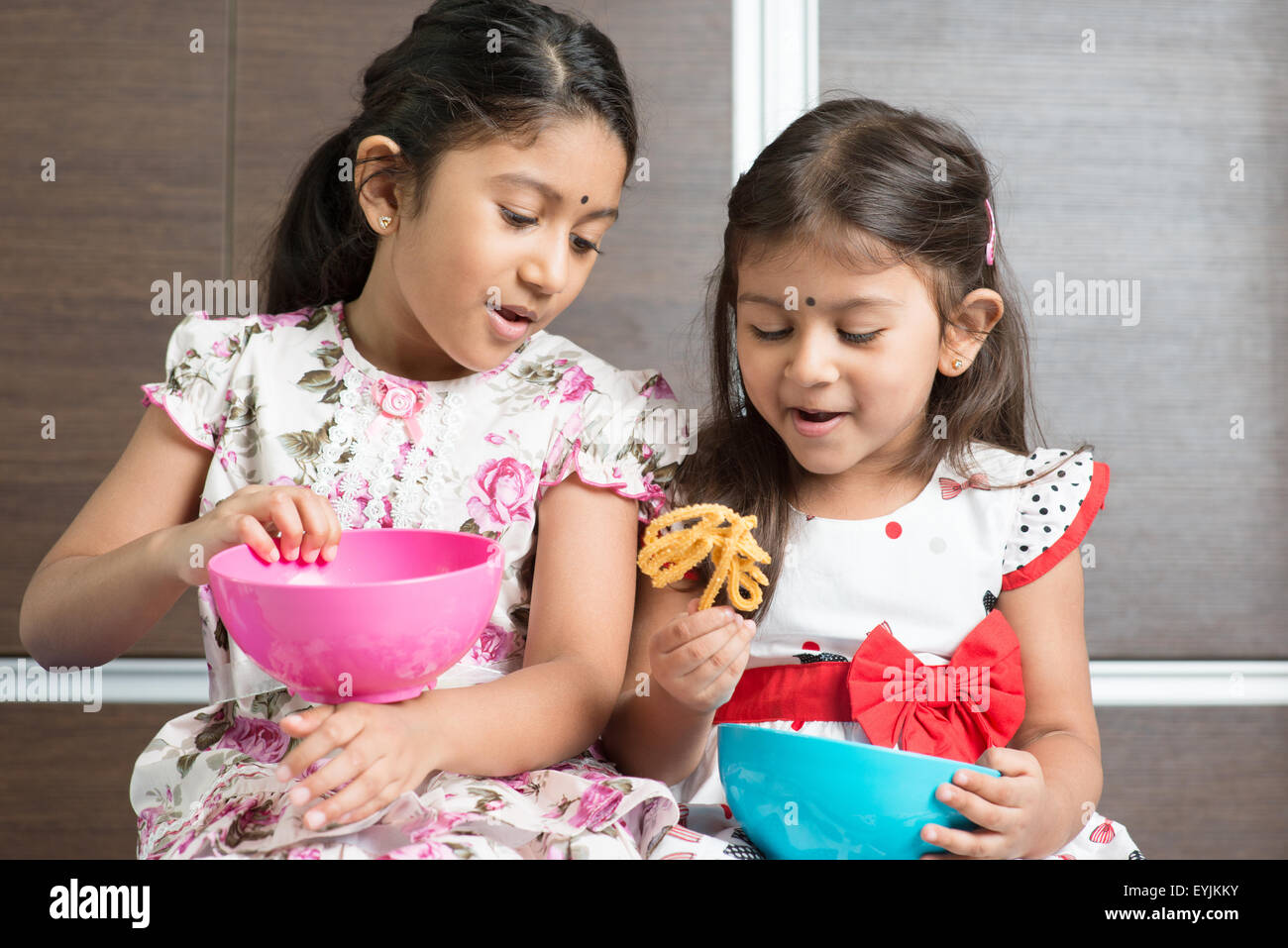 Two cute Indian girls eating traditional snack murukku. Asian sibling ...