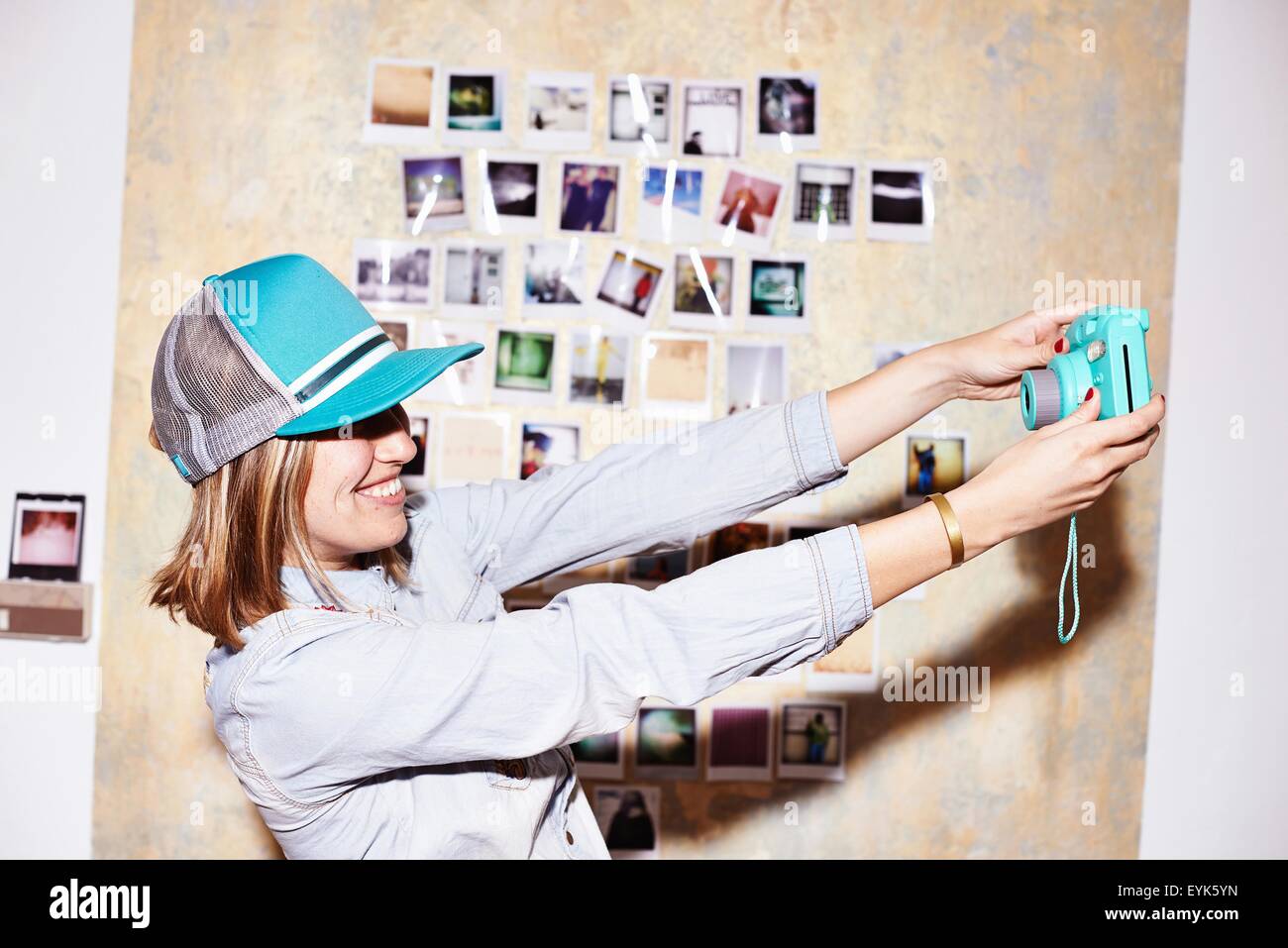 Young woman in front of photo wall taking instant selfie Stock Photo ...
