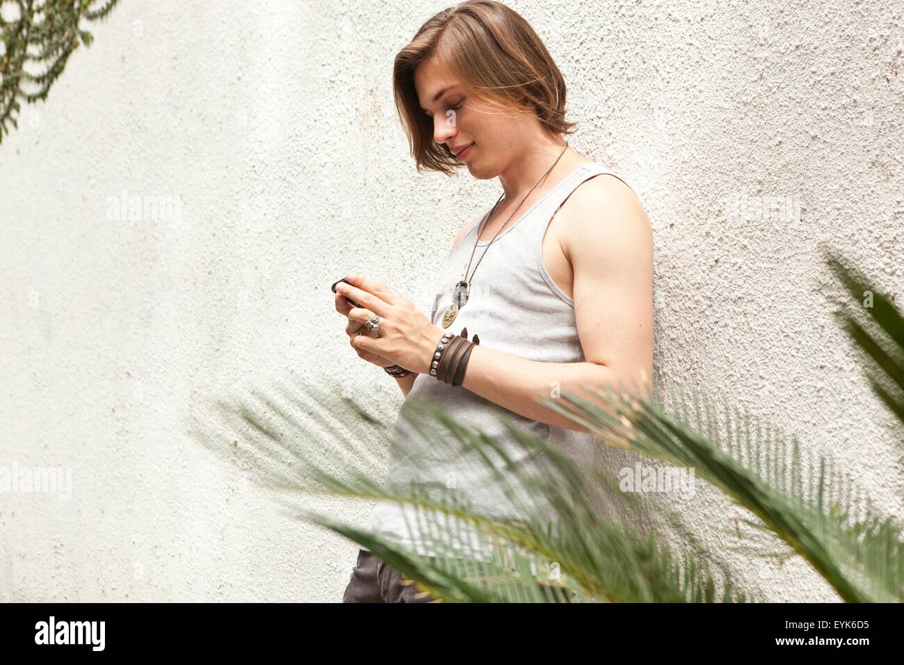 Young man leaning against wall reading text messages on smartphone ...