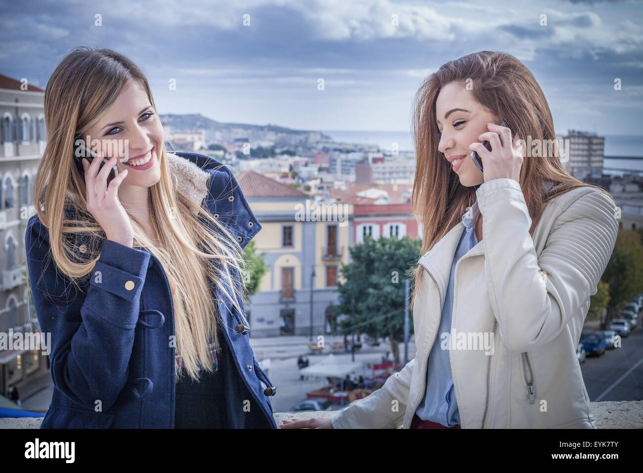 Two young women on rooftop talking on smartphones, Cagliari, Sardinia ...