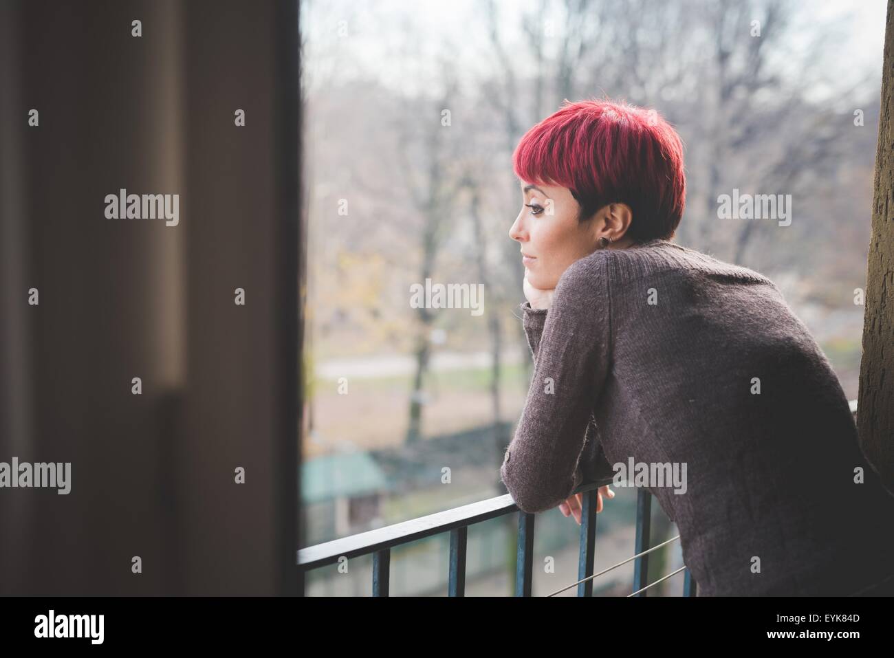 Young woman leaning against balcony railings, pensive expression Stock ...