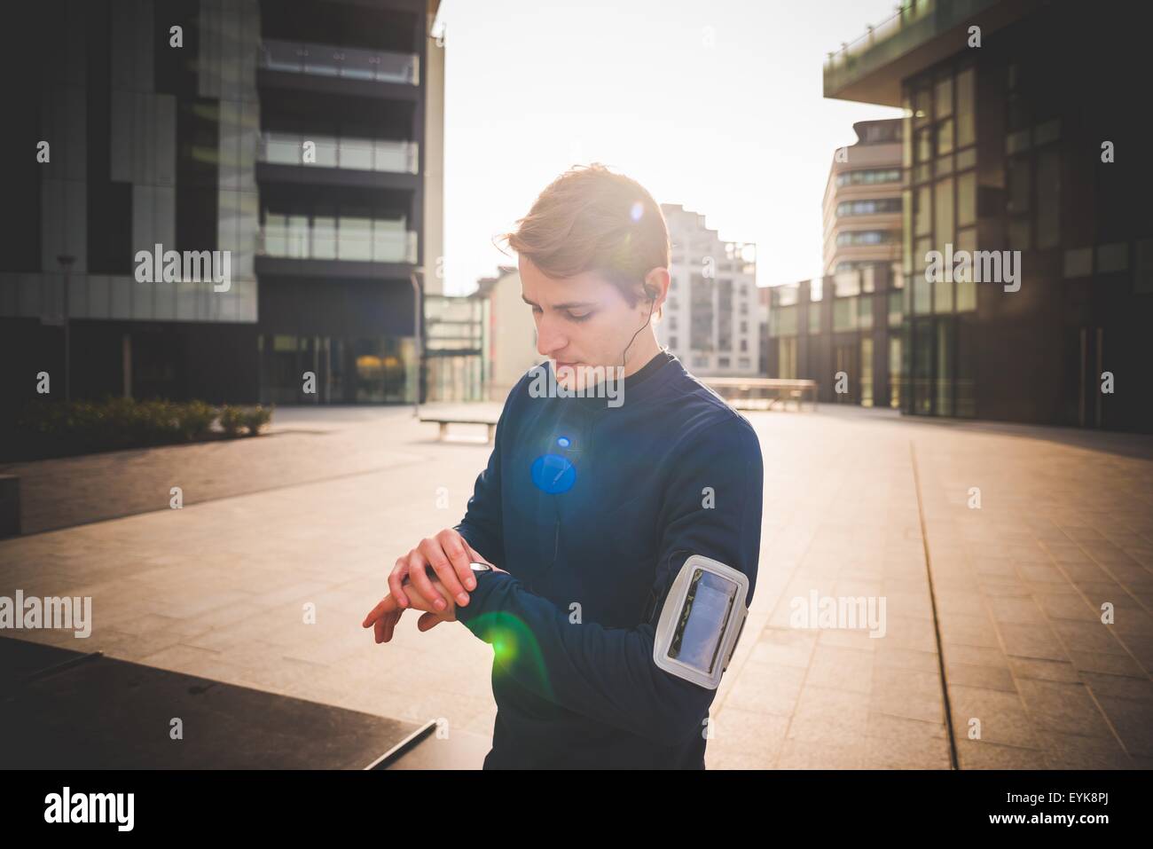 Young male runner checking wrist watch in city square Stock Photo - Alamy