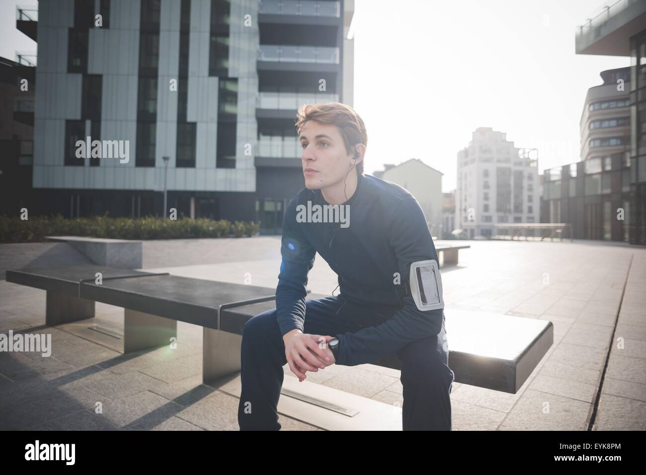 Young male runner taking a break on bench in city square Stock Photo ...
