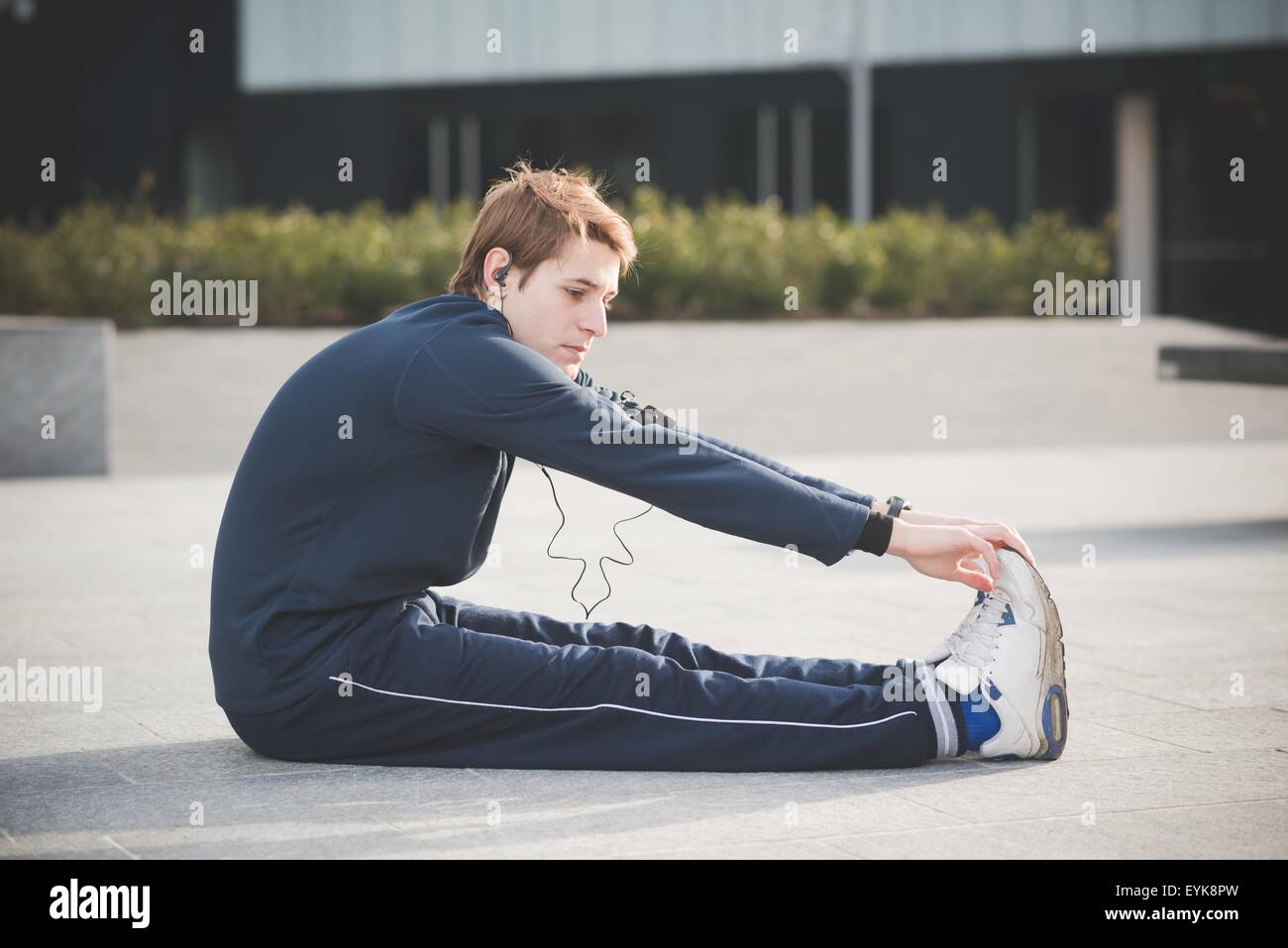 Young man touching toes in city square Stock Photo - Alamy