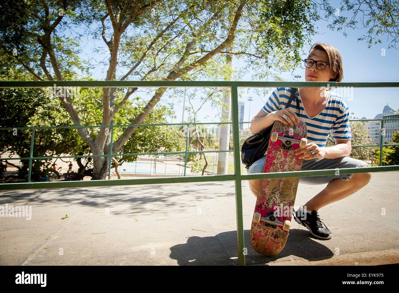 Young man holding skateboard, crouching beside railings Stock Photo - Alamy