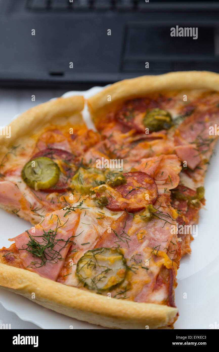 pieces pizza with sausages and bacon in plate on laptop keyboard ...