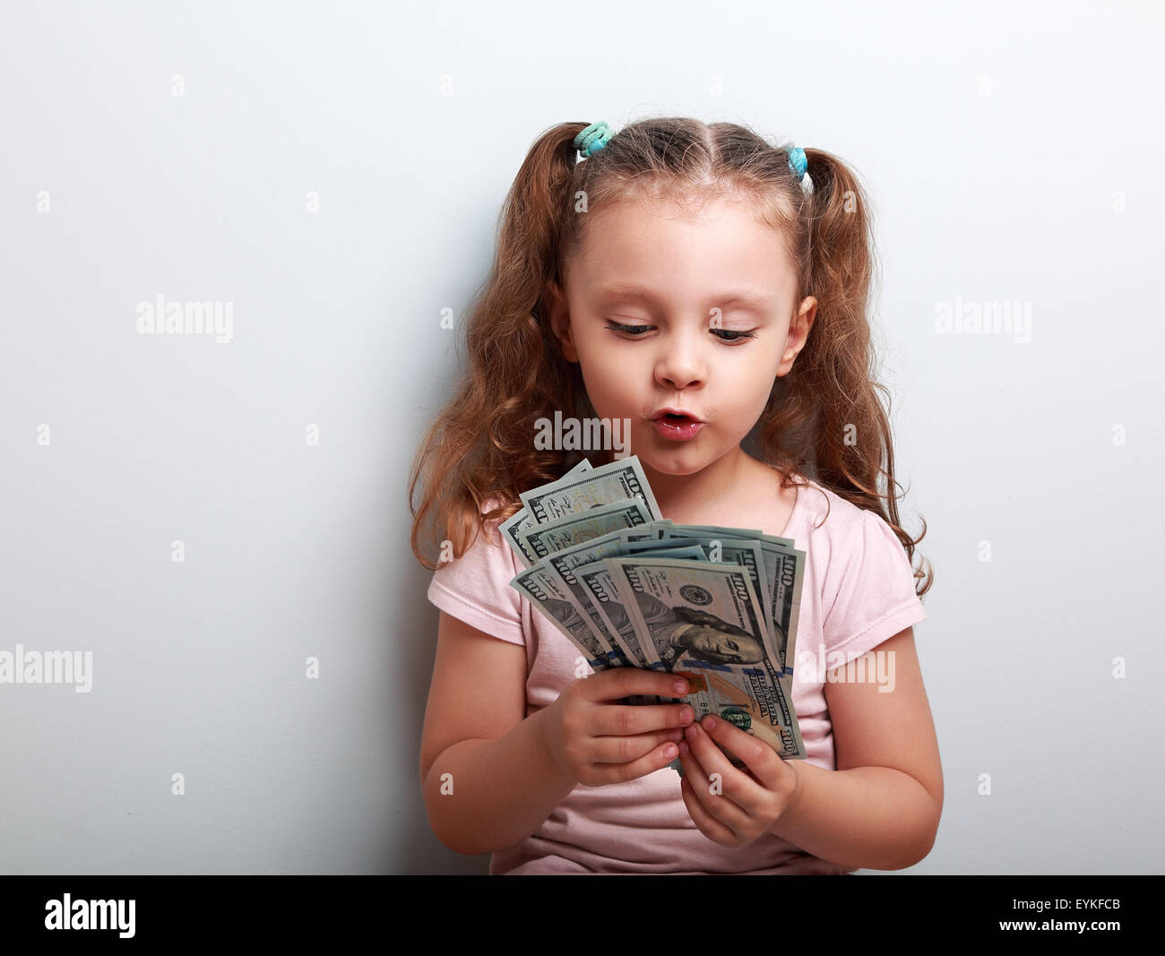 Fun grimacing kid girl looking and counting money in the hands on blue ...