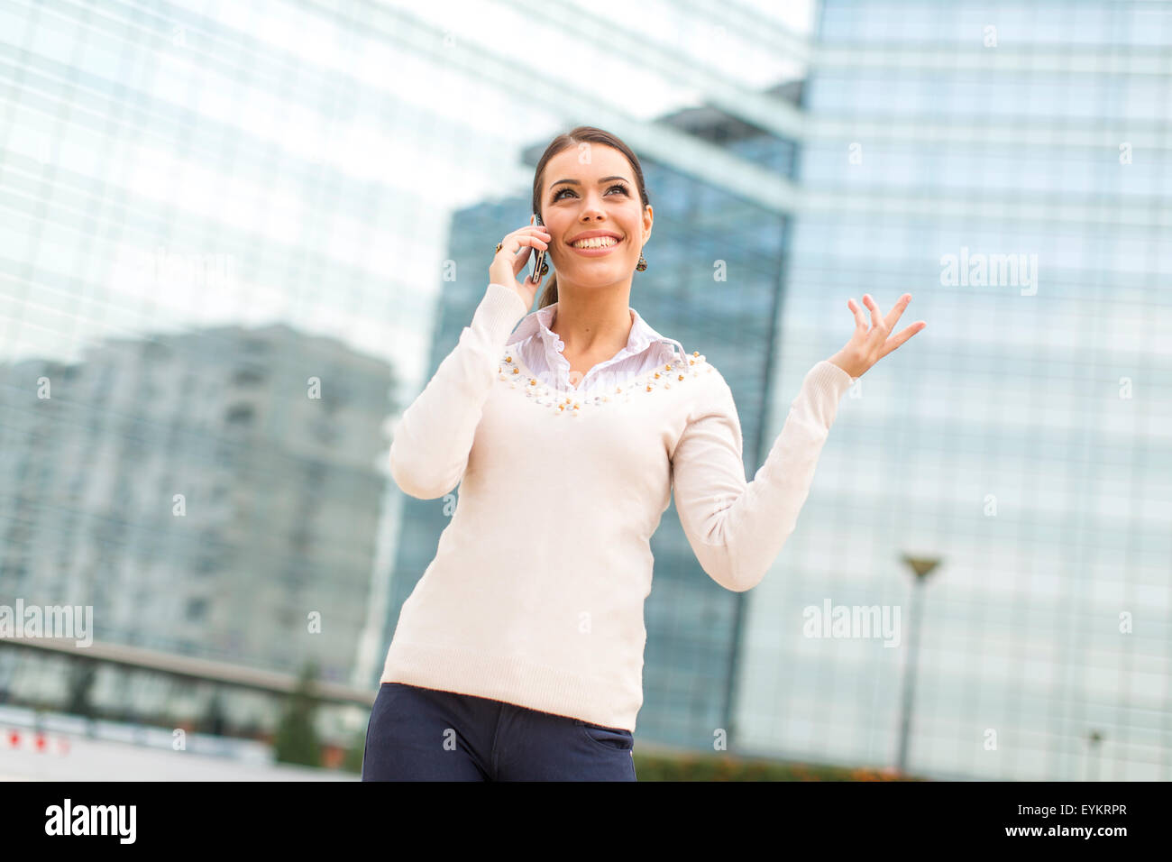 Young business woman talking on mobile phone in front of office ...
