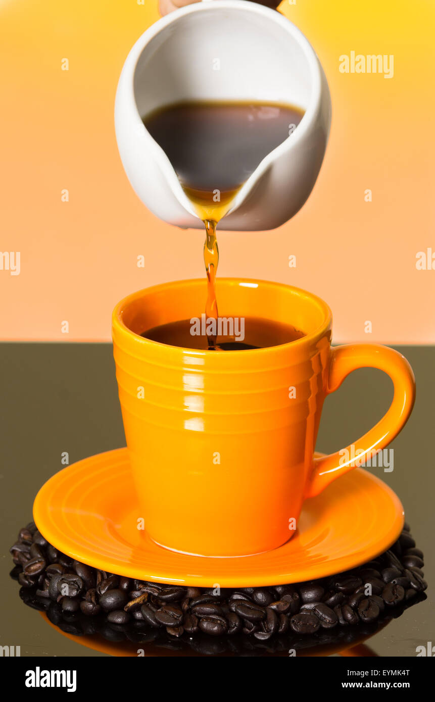 Coffee pouring from white glass kettle into colorful orange mug sitting ...