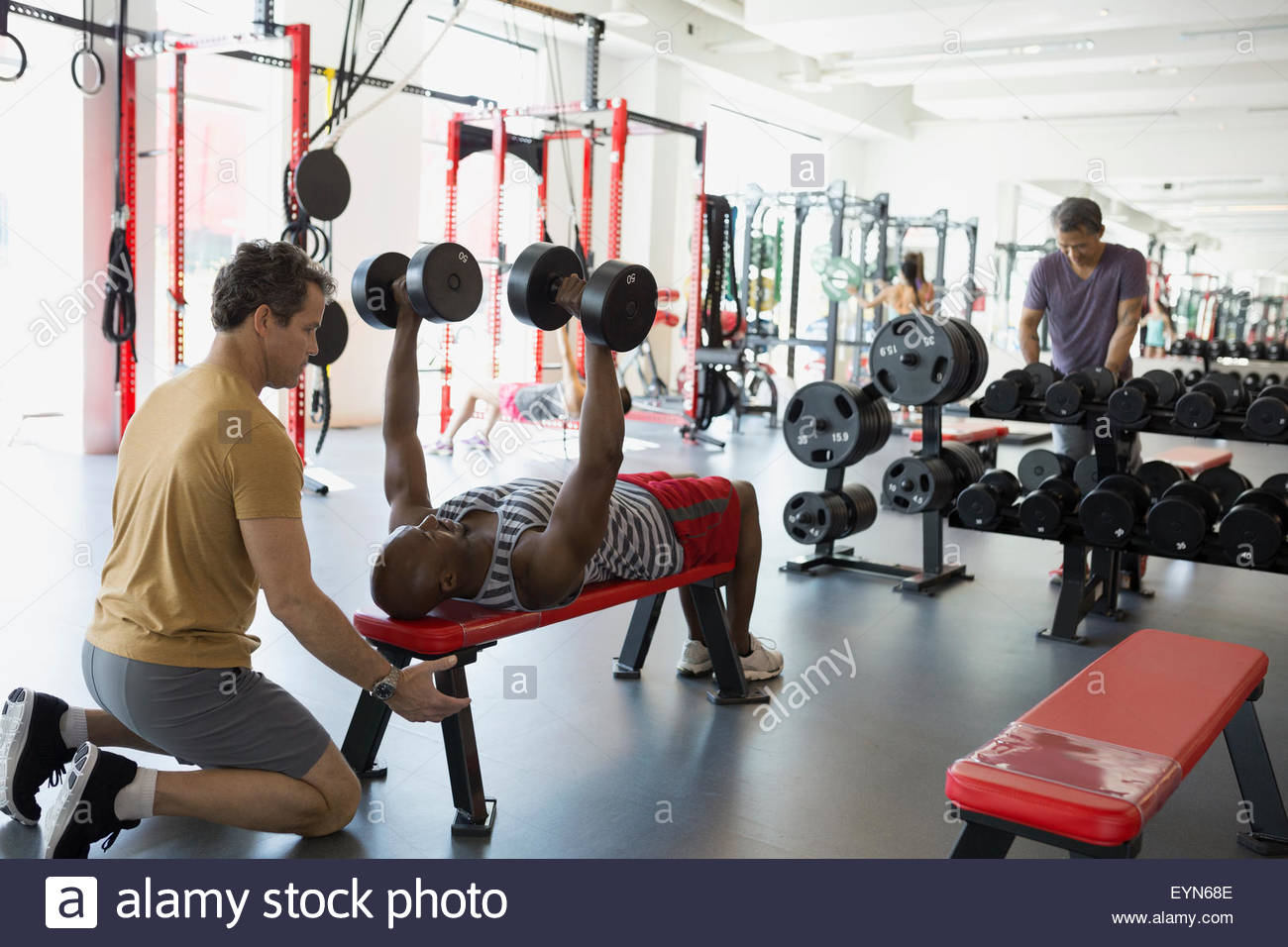 Personal trainer spotting man flat dumbbell chest press Stock Photo - Alamy