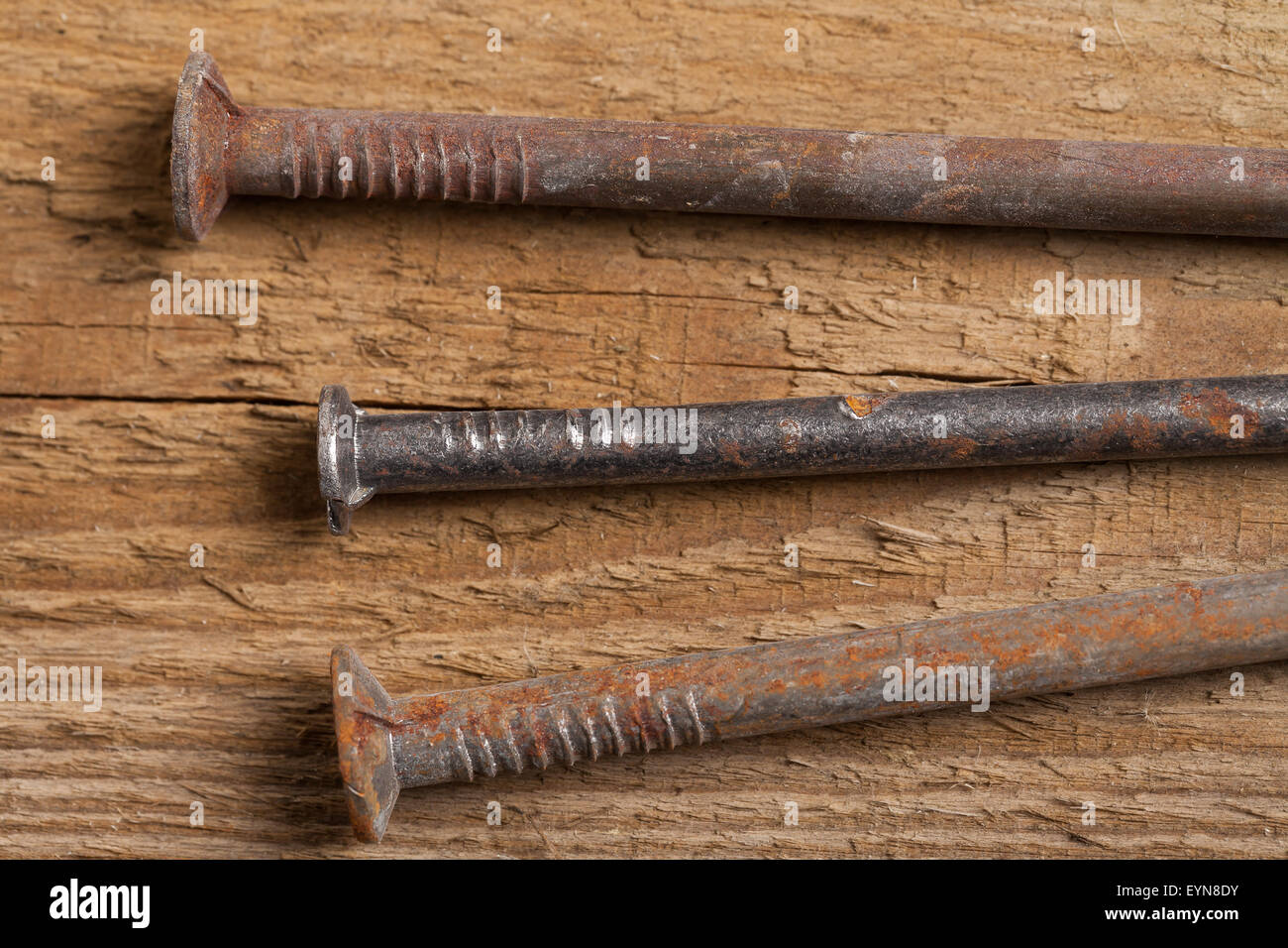 Three rusty nails on wooden board Stock Photo - Alamy