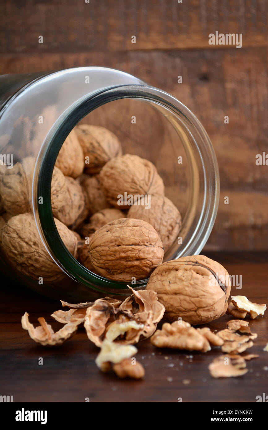 Fresh walnuts in shells falling out of glass jar on rustic dark wood ...