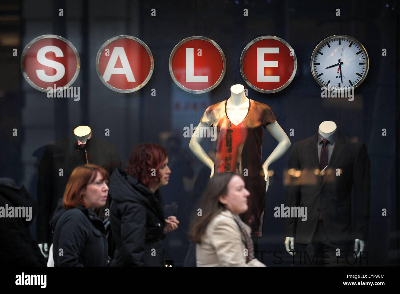 Shoppers walk in front of a high street store window with items for ...