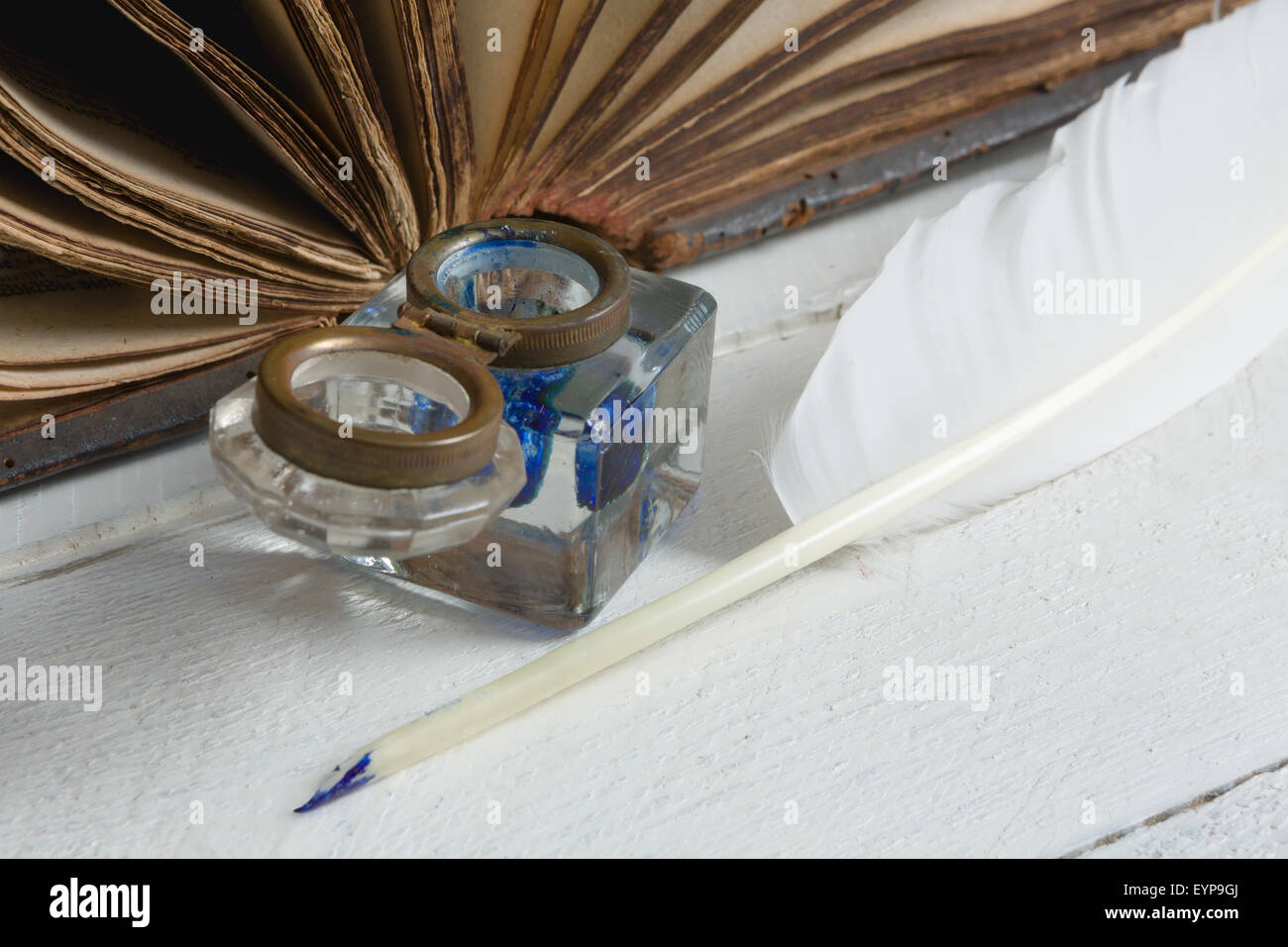 Feather quill, blue ink pot and medieval book on a rustic white painted ...