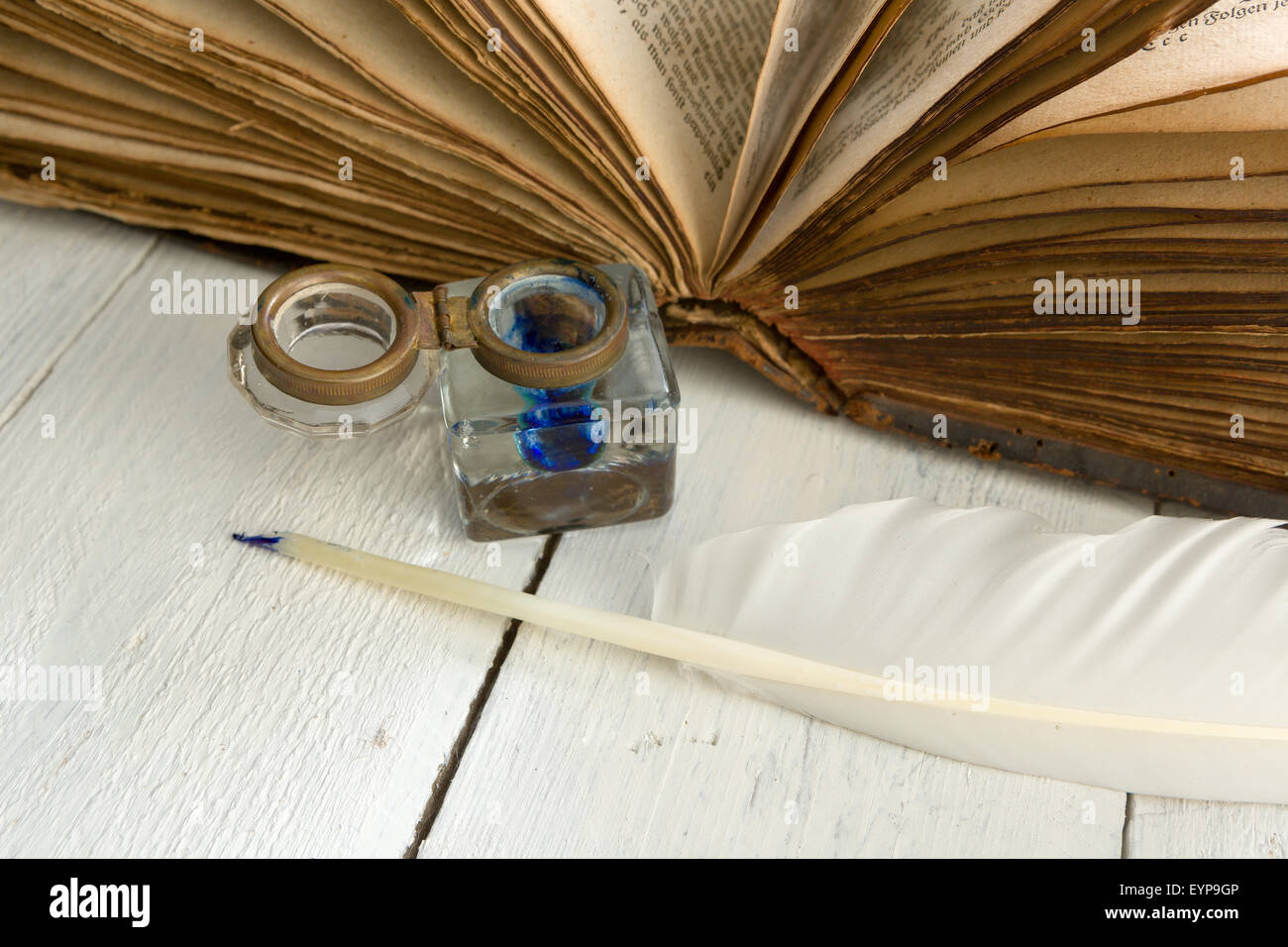 Feather quill, blue ink pot and medieval book on a rustic white painted ...