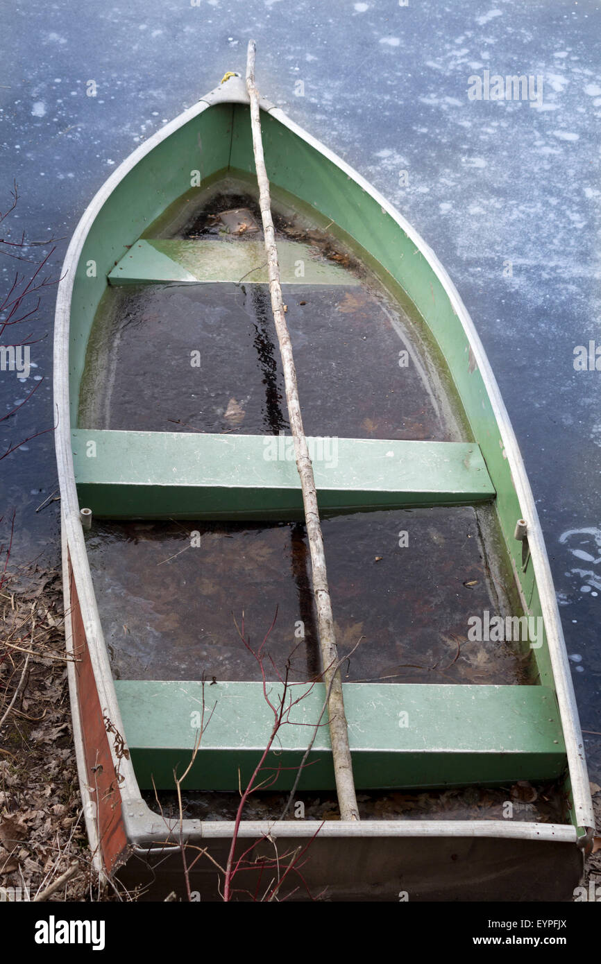 Abandoned boat filled with dirty water sitting on shore partly in water ...