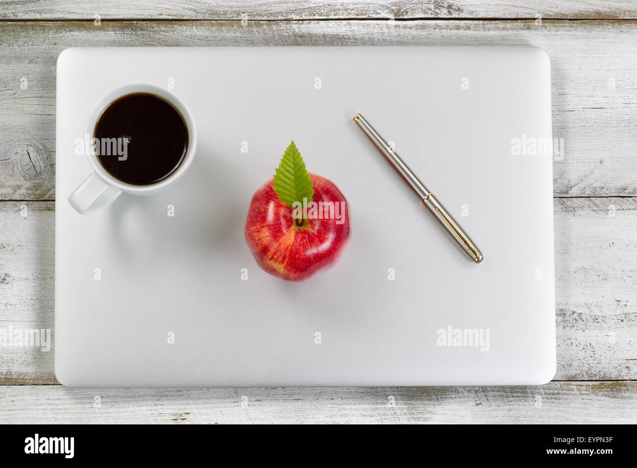Red apple, coffee and silver pens on top of laptop with rustic white desktop in background Stock ...