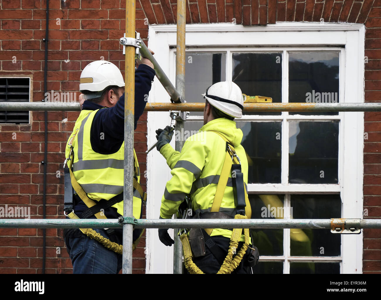 Two workers assembling scaffolding on city building Stock Photo - Alamy