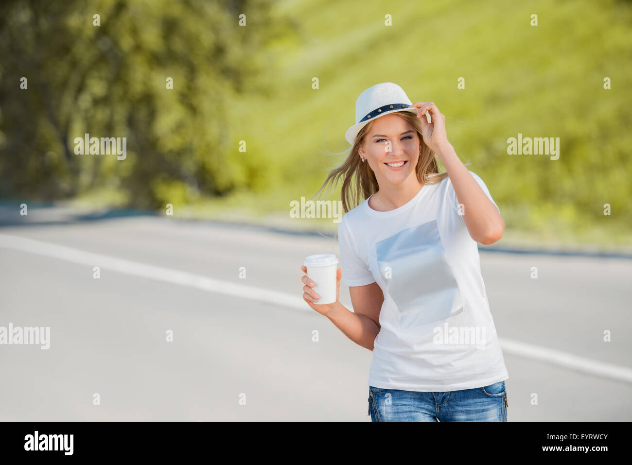 Beautiful young woman with a disposable coffee cup, walking along the ...