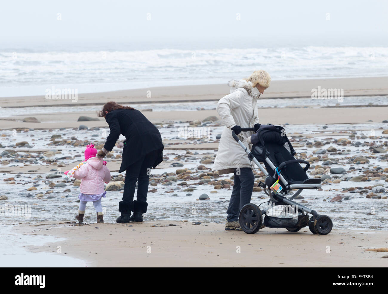 Two women an child on beach on a cold, stormy March day. England. UK ...