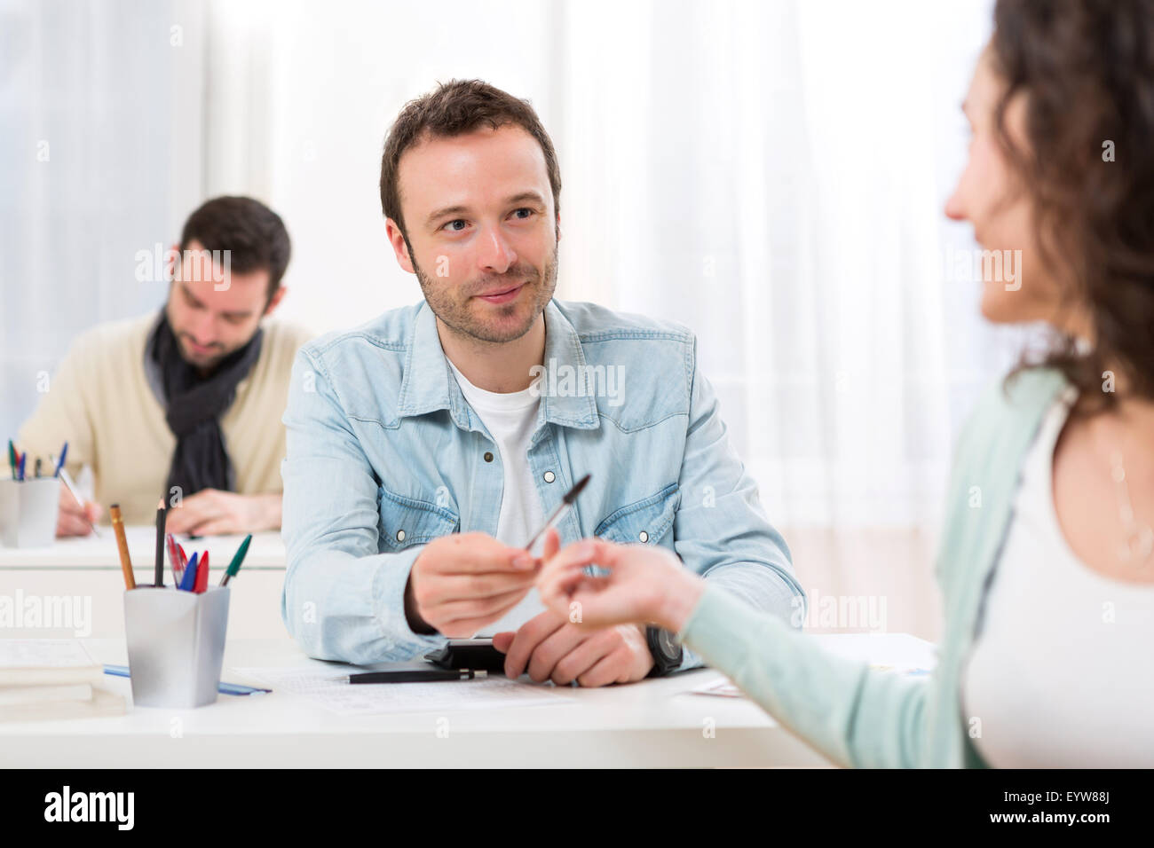 View of a Young attractive student lend a pen to classmate Stock Photo ...