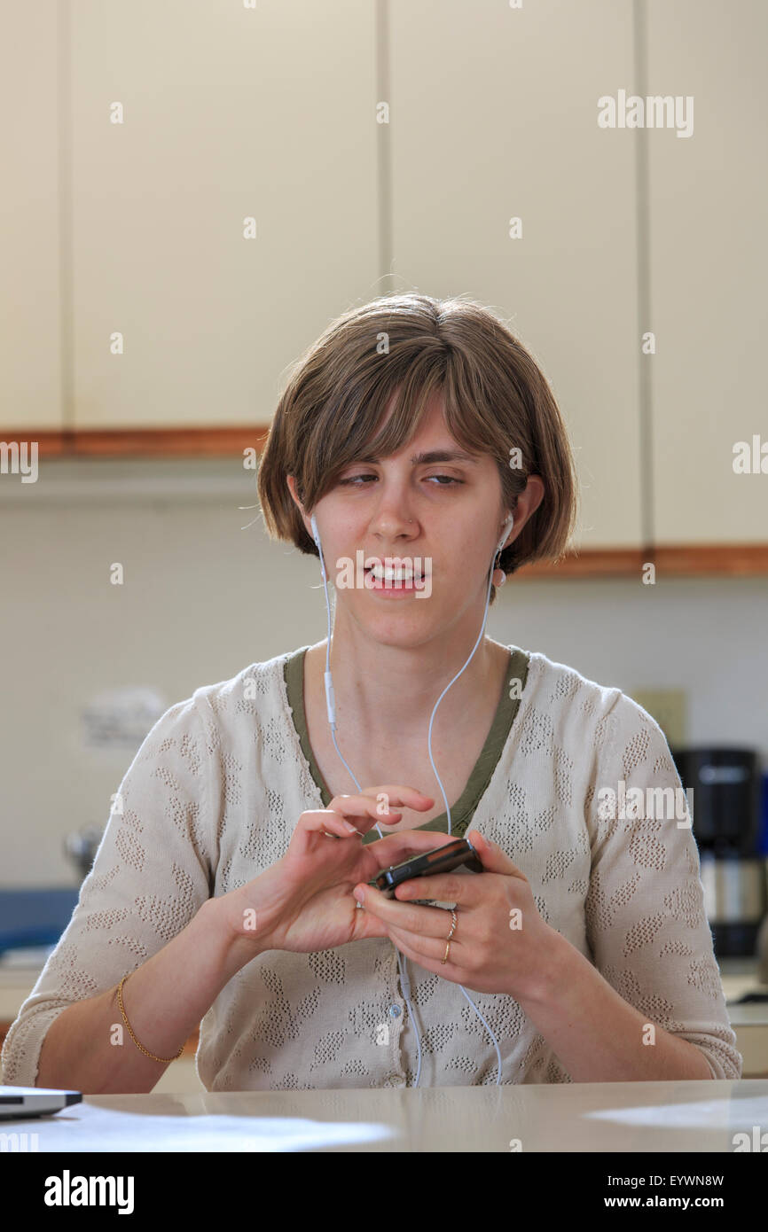 Blind woman using assistive technology ear plugs to listen to her cell ...