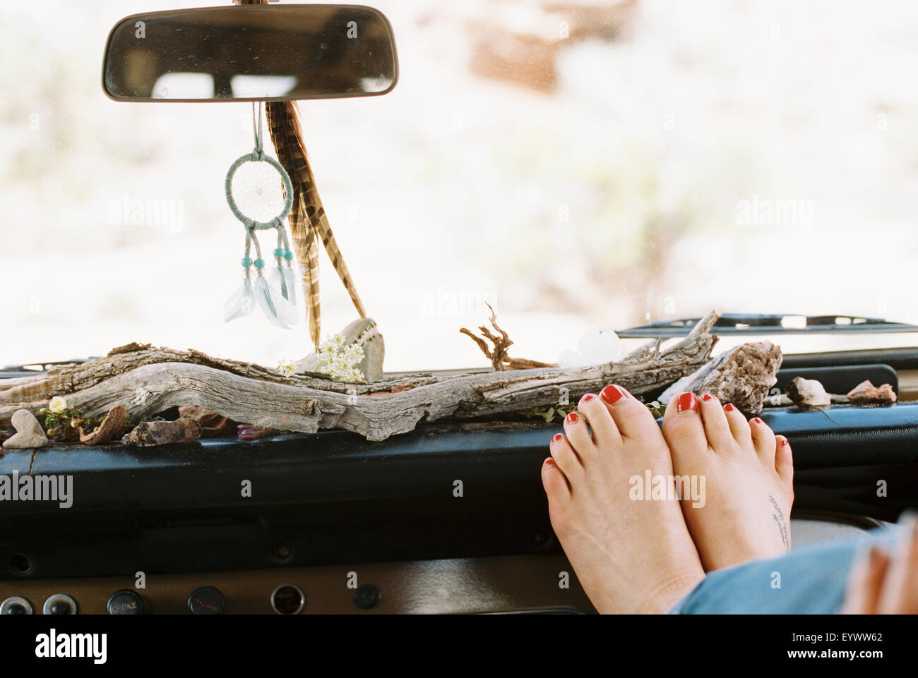 A woman resting her bare feet on the dashboard of a 4x4, on a road trip ...